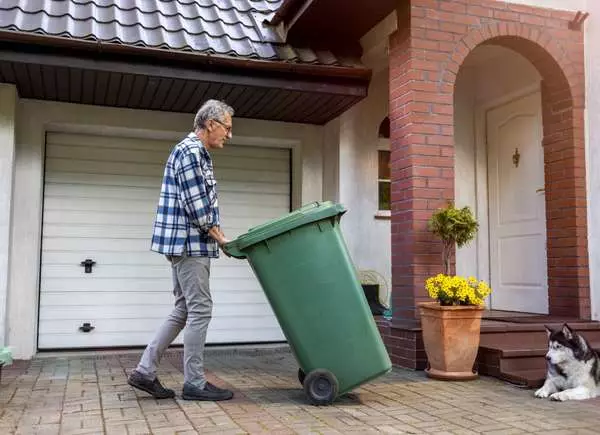 Bărbat în vârstă care scoate un coș de gunoi