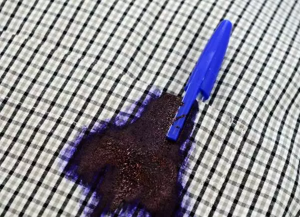 Primul plan al unei pate de cerneală de stilou albastru pe o cămașă în carouri