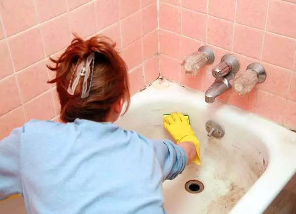 Záber zhora, ako niekto čistí špinavú vaňu v kúpeľni s ružovými keramickými dlaždicami