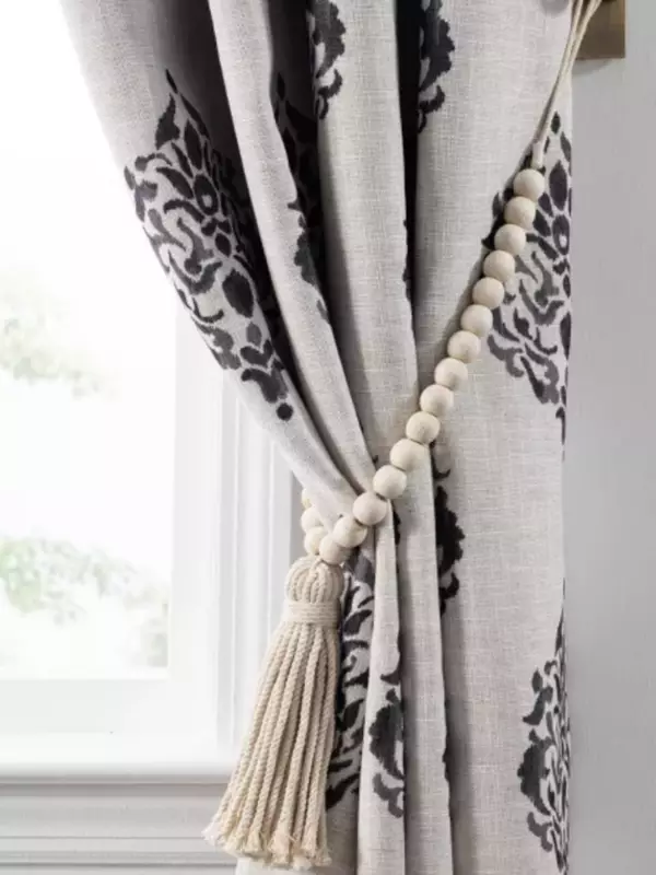 Beige Perlen, die einen grau/weiß geblümten Vorhang hinter einem weiß gerahmten Fenster halten