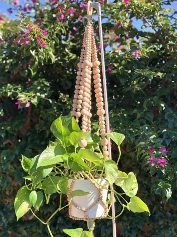 Perlenkette, die draußen eine Pflanze in einem weißen Topf hält