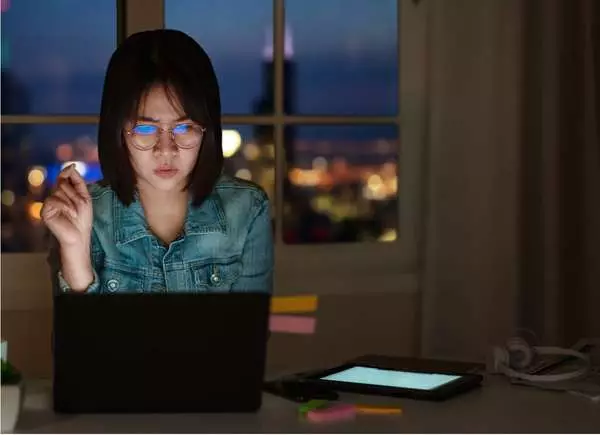 Wanita yang duduk di depan laptop bekerja, di belakangnya Anda dapat melihat langit malam