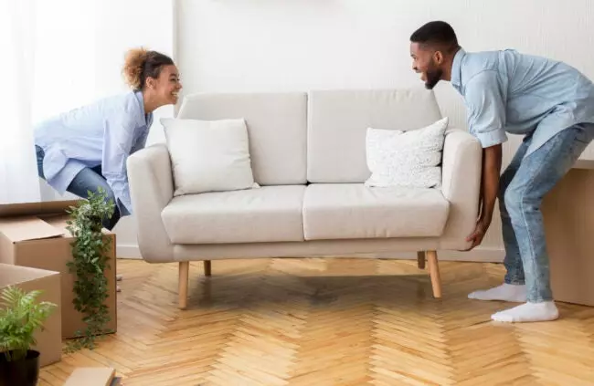 Переміщення концепції. Веселий афро-подружжя розставляють диван у порожній кімнаті в новому будинку після переїзду