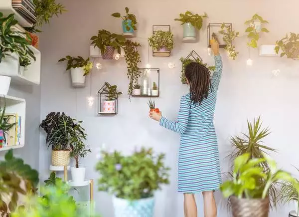 Kvinna vänd mot väggen vattna krukväxter mot en vägg