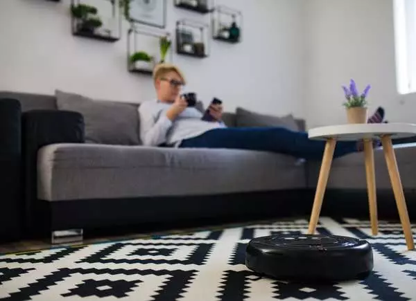 Femme se relaxant pendant que le robot aspirateur nettoie