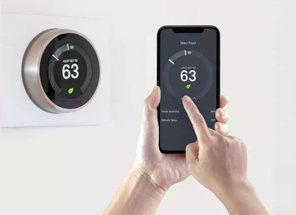Išmanusis termostatas fone ir telefonas priekiniame plane – abu rodo 63 laipsnius