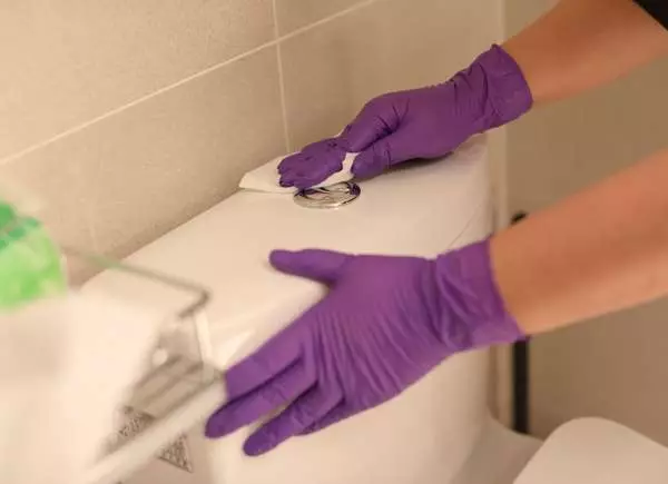 Людина в фіолетових гумових рукавичках чистить верхню частину туалету