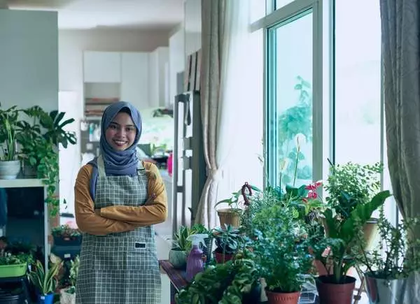실내의 많은 식물 앞에 서 있는 히잡을 쓴 여자