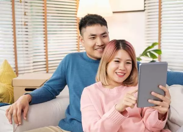 Asiatische Paare, die ein iPad betrachten, das auf dem Sofa sitzt